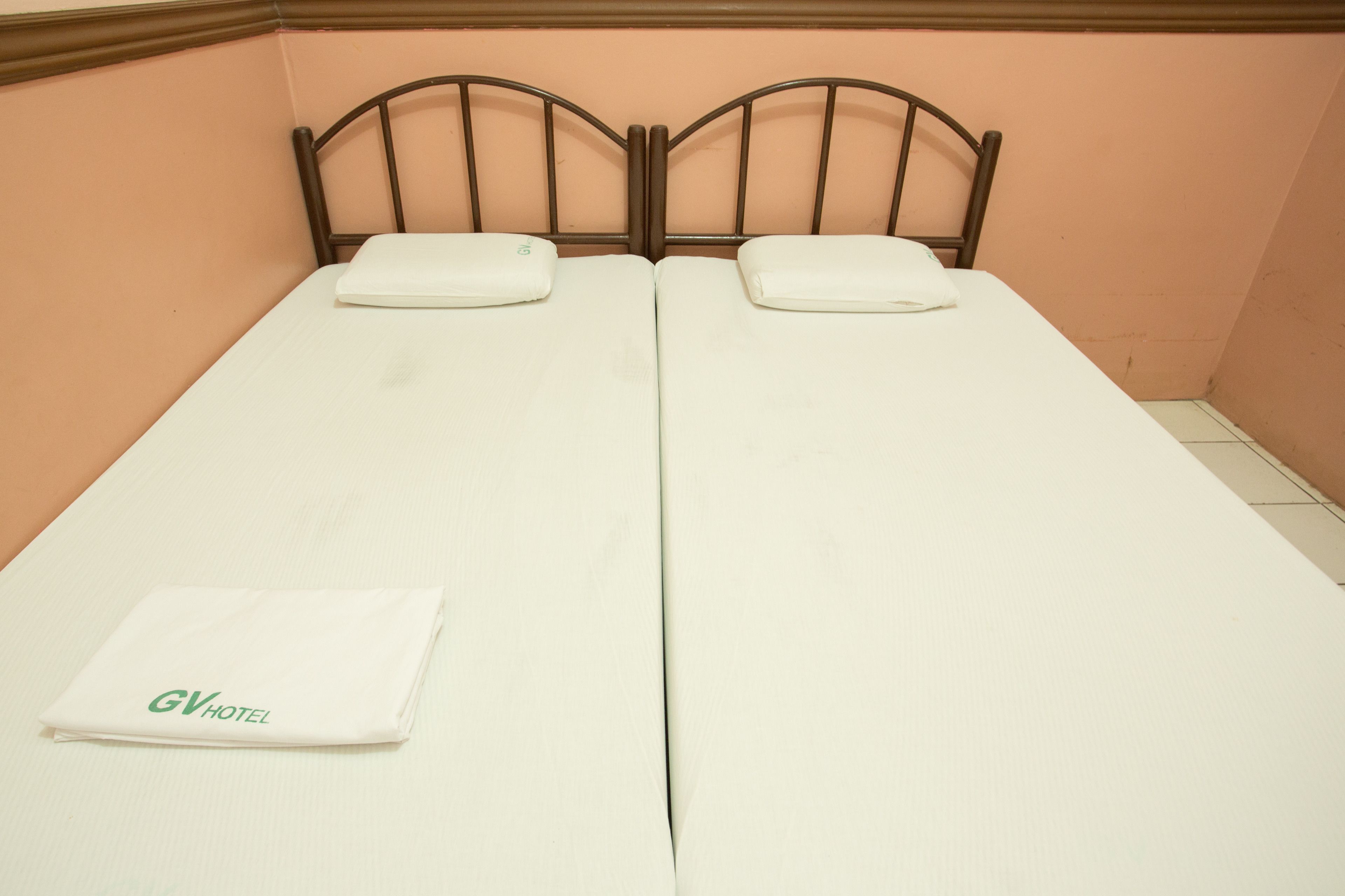 Uma cama de casal com cabeceira, uma toalha branca dobrada e uma placa com a inscrição "GV Hotel" sobre a cama.