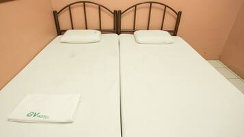 Uma cama de casal com cabeceira, uma toalha branca dobrada e uma placa com a inscrição "GV Hotel" sobre a cama.