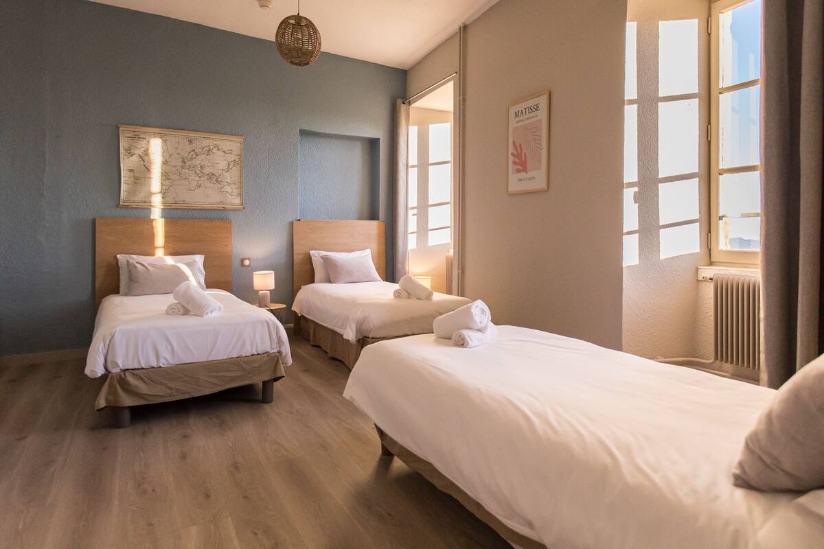 Quarto de hotel com três camas, um mapa na parede e uma janela com cortinas.