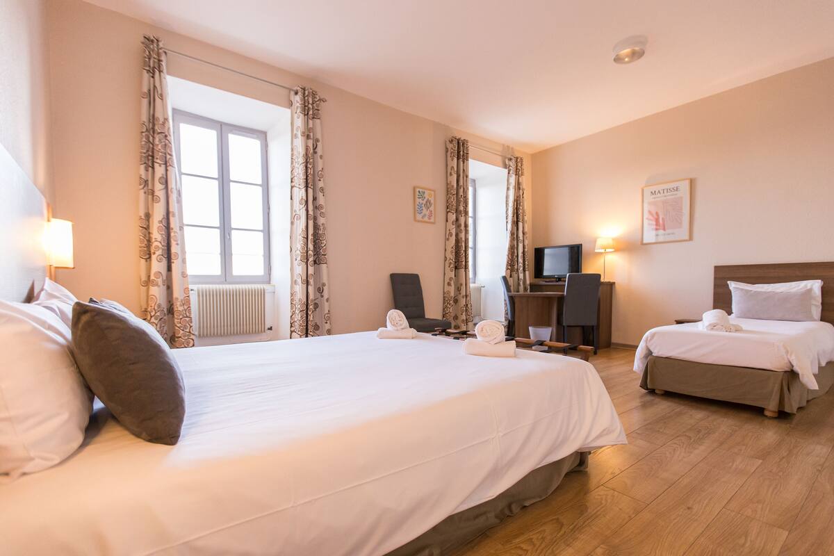 Quarto de hotel com duas camas, uma escrivaninha, uma cadeira, uma televisão e um radiador.