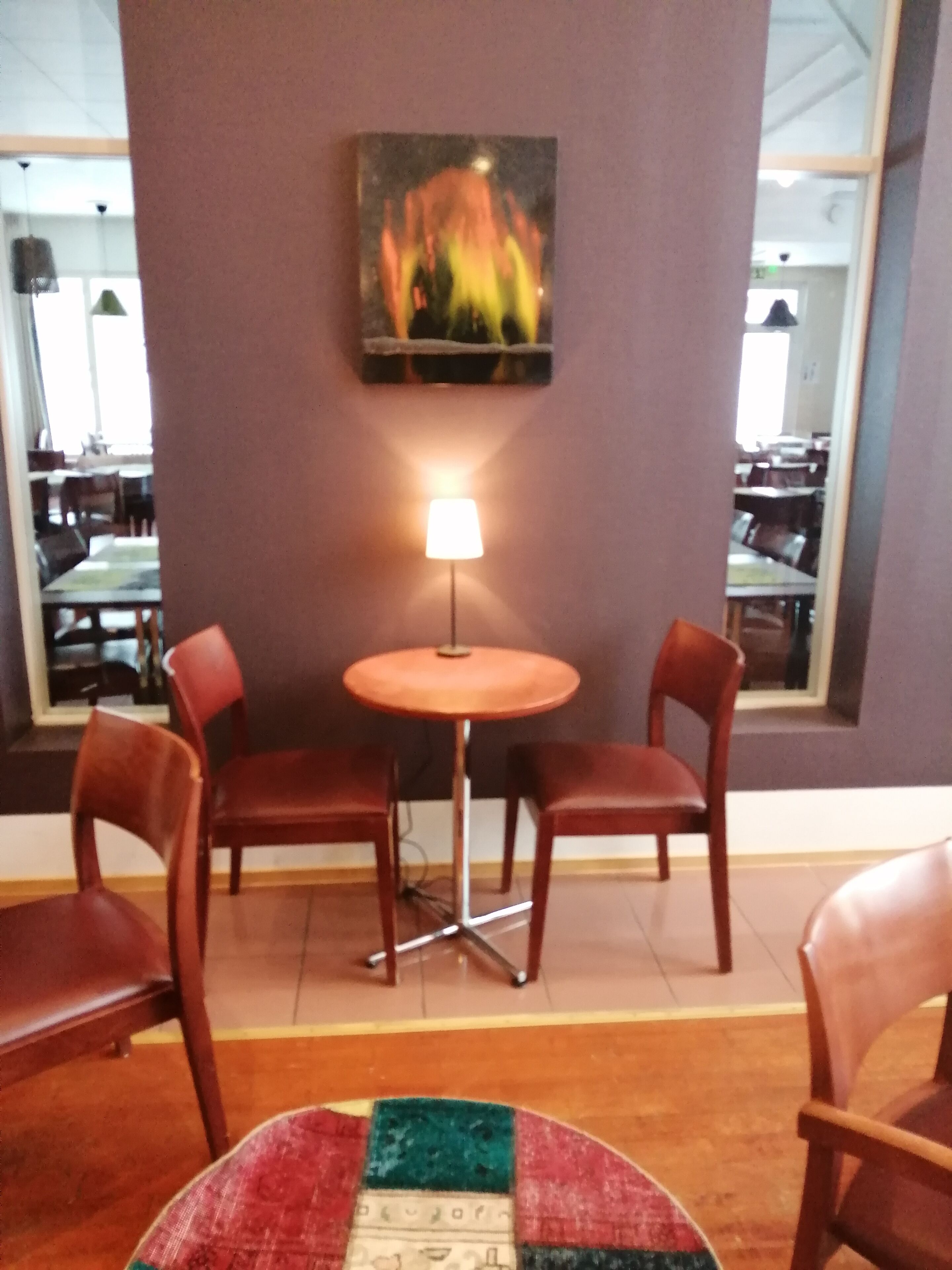 Uma área de refeições com uma mesa redonda e quatro cadeiras, uma luminária na parede e um quadro de uma lareira.