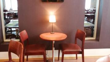 Uma área de refeições com uma mesa redonda e quatro cadeiras, uma luminária na parede e um quadro de uma lareira.