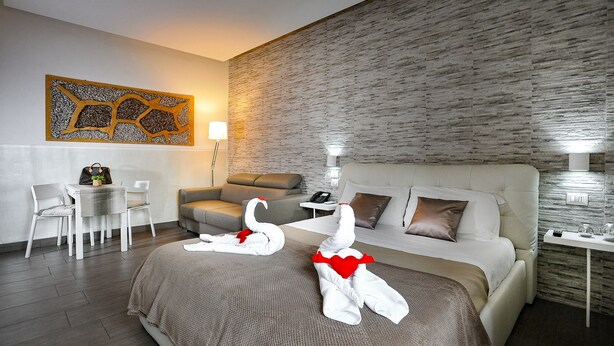Quarto de hotel moderno com cama, sofá, escrivaninha e cadeira. Há duas toalhas em forma de cisne sobre a cama.