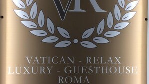 A sign with the logo "VR" surrounded by a laurel wreath, and text stating "VATICAN - RELAX LUXURY - GUESTHOUSE ROMA".