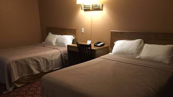 Quarto de hotel com duas camas, uma escrivaninha com telefone e uma luminária na parede.