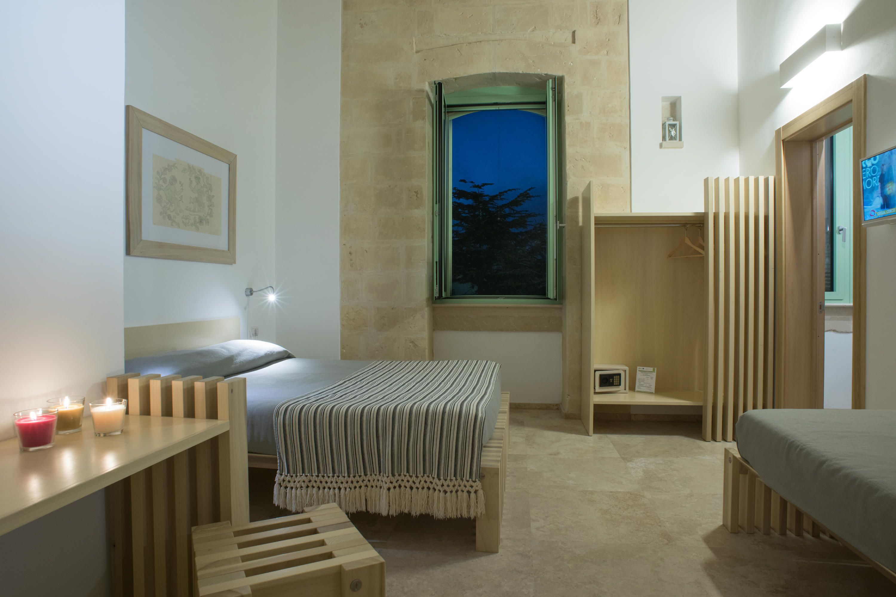 Quarto moderno com cama, mesa de cabeceira com velas, janela com vista para árvores e guarda-roupa de madeira.
