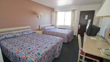 Quarto de hotel com duas camas, uma escrivaninha, uma cadeira, um abajur e uma janela.