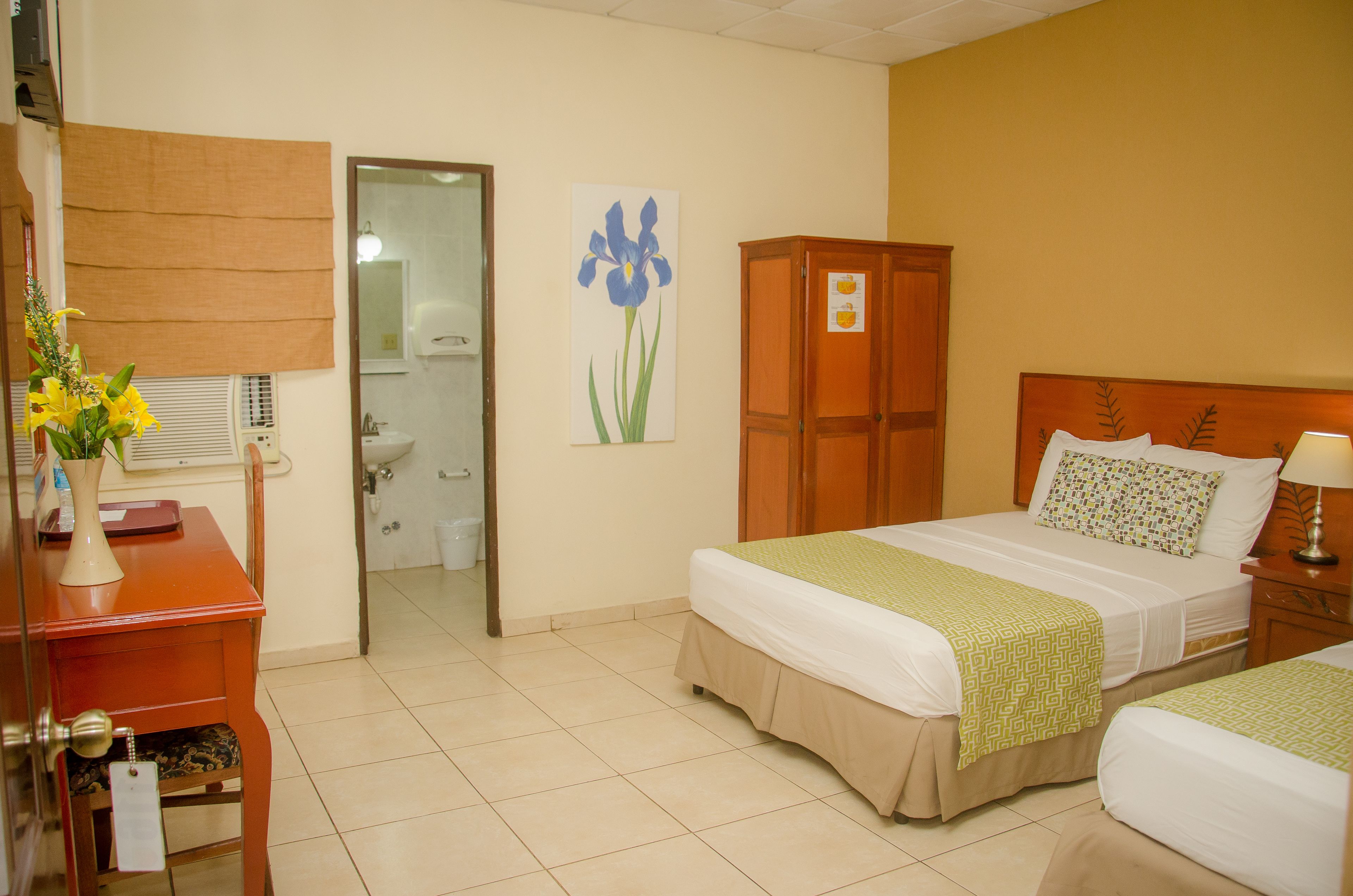 Quarto de hotel com duas camas, um guarda-roupa de madeira, casa de banho com sanita e lavatório, e uma porta que dá para a casa de banho.