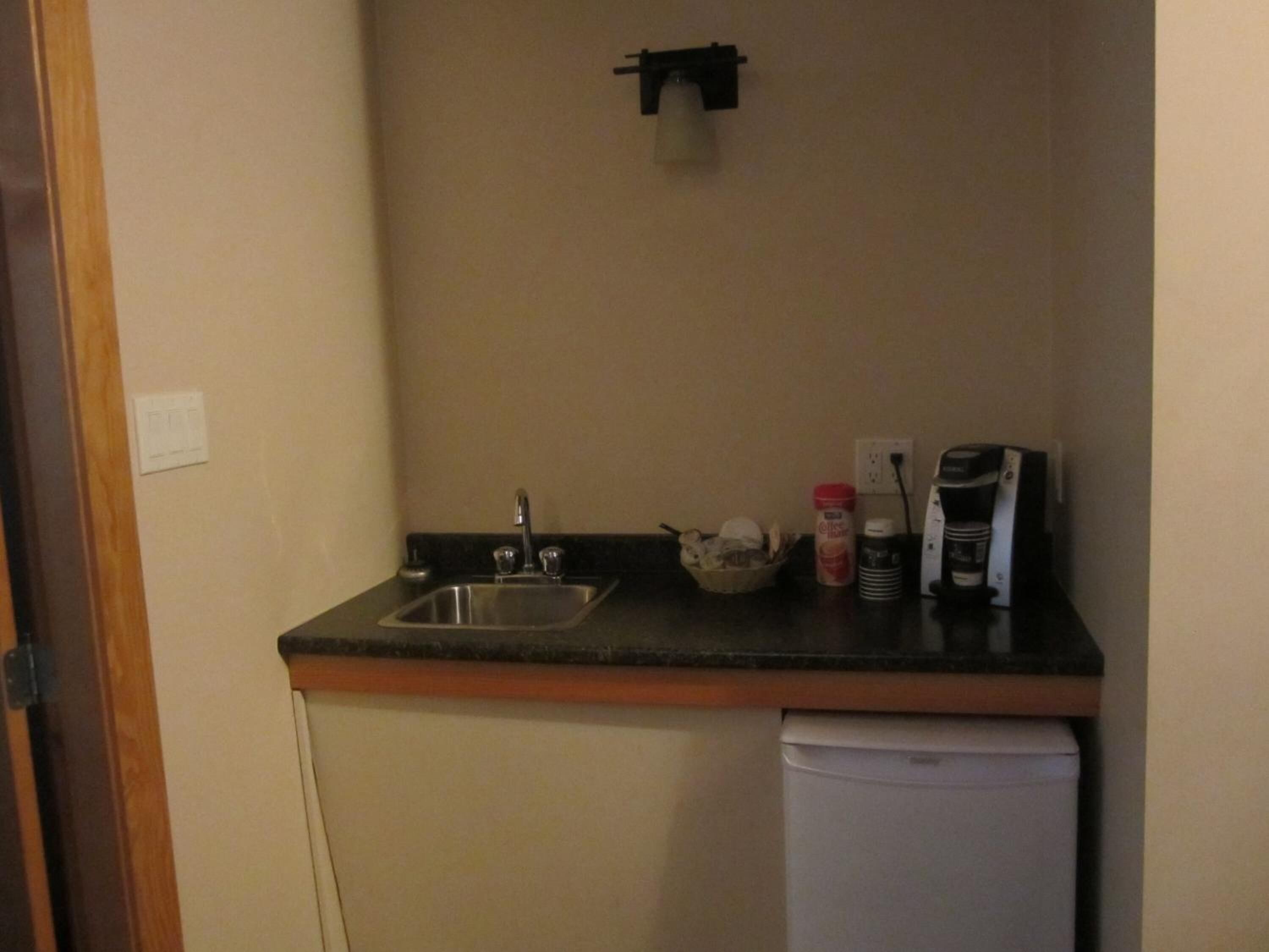 Uma cozinha compacta equipada com pia, cafeteira e pequeno frigorífico.