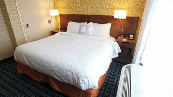 Quarto de hotel com uma cama grande, duas luminárias de cabeceira, um criado-mudo e um ar condicionado fixado na parede.