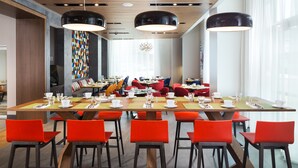Uma zona de refeições moderna com uma mesa comprida, cadeiras vermelhas e luminárias pendentes pretas.