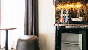Quarto de hotel com bancada de mármore, minibar e um banquinho de couro.