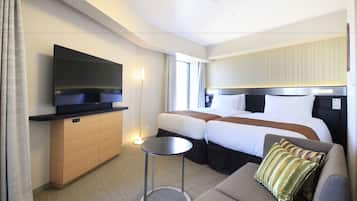 Quarto de hotel com cama, sofá, televisão em móvel, mesinha e janela com cortinas.