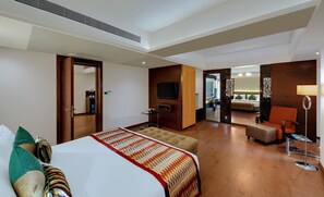 Quarto de hotel moderno com uma cama grande, televisão, escrivaninha e área de estar.