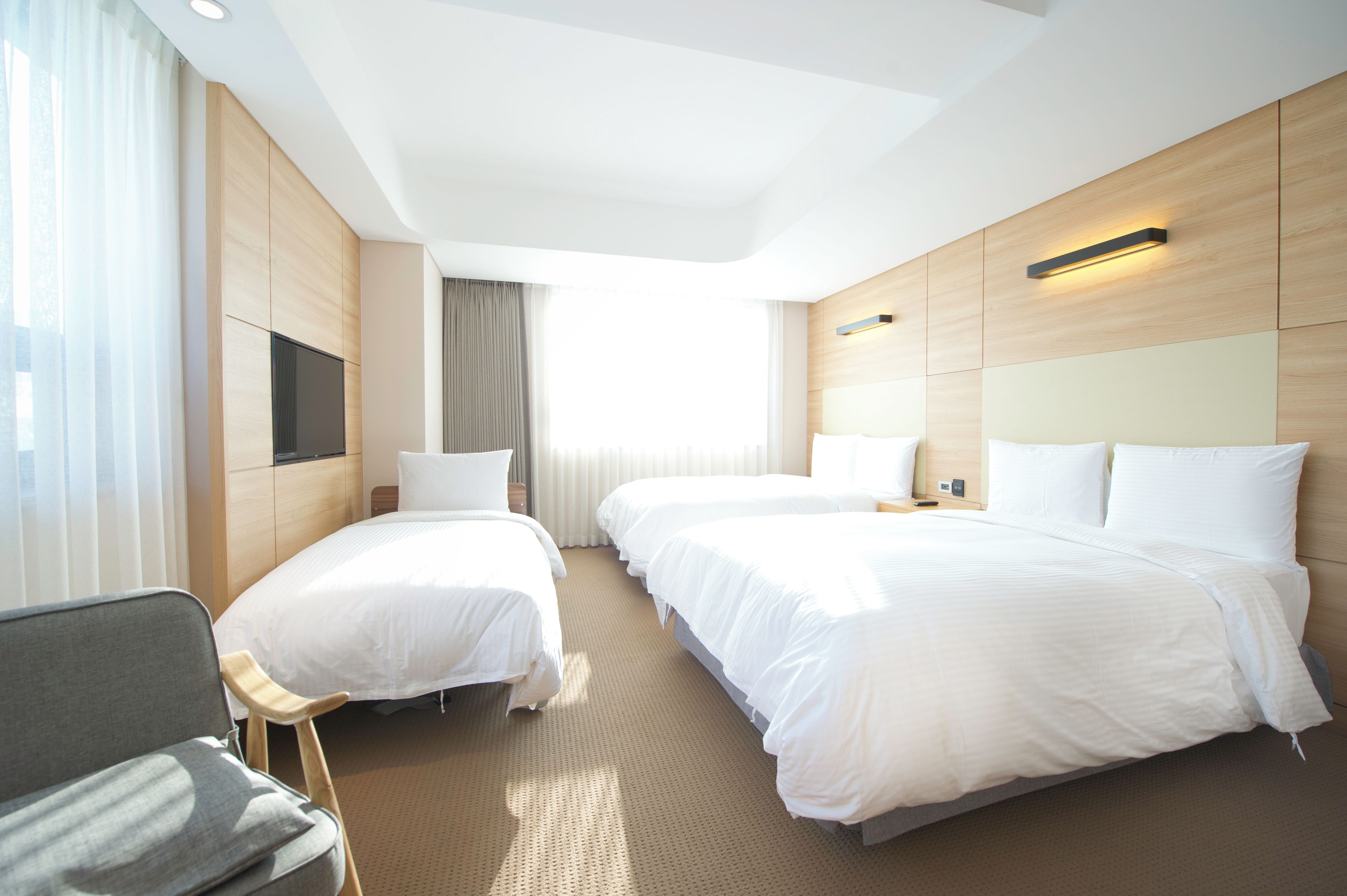 Quarto de hotel com duas camas, um sofá, uma televisão e uma janela grande com cortinas.