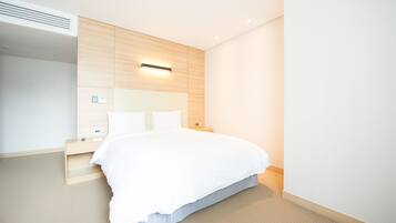 Quarto de hotel moderno com uma cama grande, painéis de parede de madeira, uma mesa de cabeceira e unidade de ar condicionado embutida.