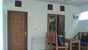 Quarto com porta de madeira, radiador de metal, mesa de madeira com cadeira e janela com vista para área verde.
