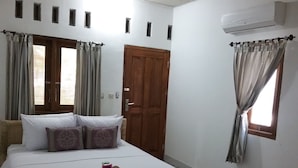 Quarto de hotel com cama, cortinas, porta de madeira e aparelho de ar condicionado.