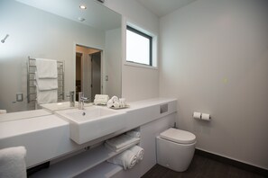 Uma casa de banho moderna com um espelho grande, duas pias, uma sanita e um porta-toalhas.
