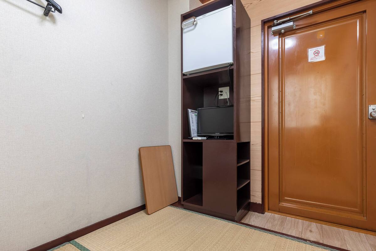 Um quarto com porta de madeira, estante com televisão e chão de esteira de tatame.