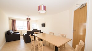 Uma sala de estar moderna com uma mesa de jantar, cadeiras, um sofá e uma televisão.