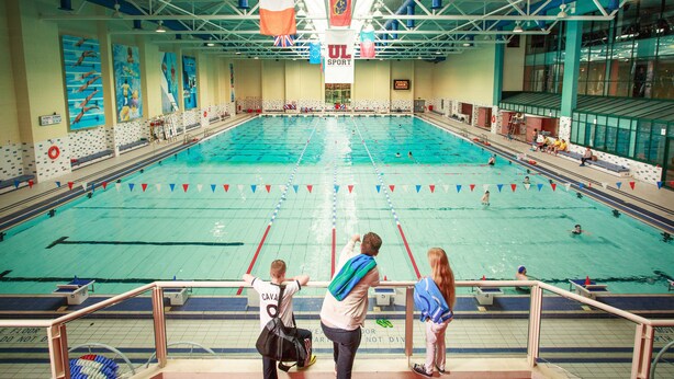 Piscina interna com várias pistas de natação, cadeiras de salva-vidas e área com carpete vermelho.