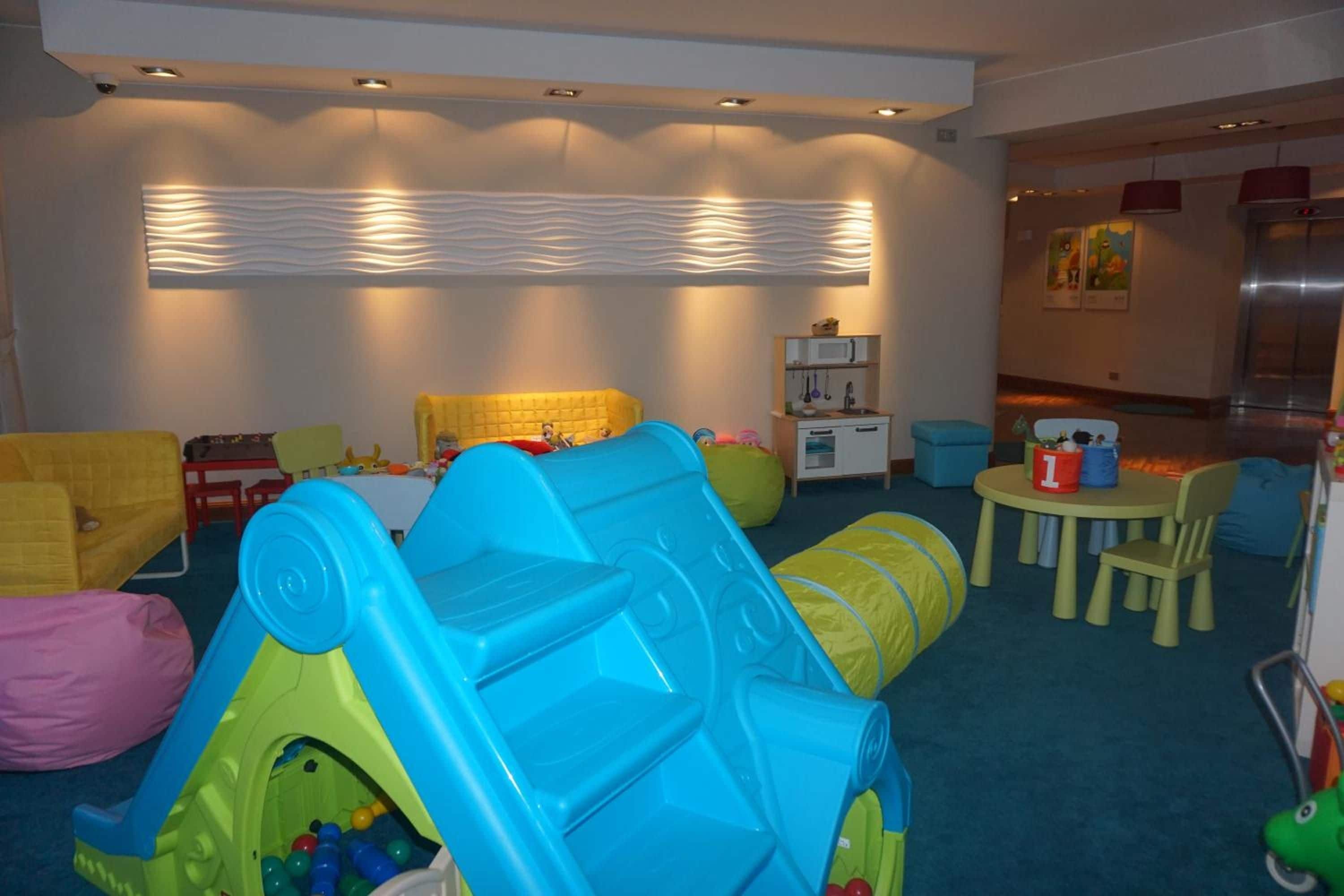 Espaço de recreação infantil com escorrega, almofadas de diversos tons e uma pequena copa.