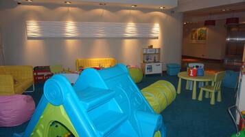 Espaço de recreação infantil com escorrega, almofadas de diversos tons e uma pequena copa.