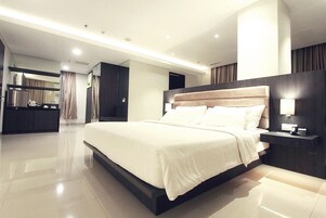 Quarto de hotel moderno com uma cama grande, banheiro separado e área de cozinha compacta.