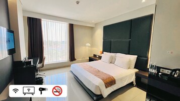 Quarto de hotel com cama, escrivaninha, cadeira, televisão, abajur e vista para o exterior pela janela.