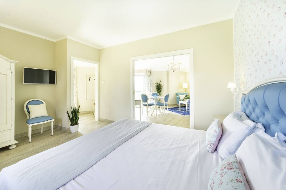 Quarto com cama grande, televisão, cadeira e pequena mesa com cadeiras.