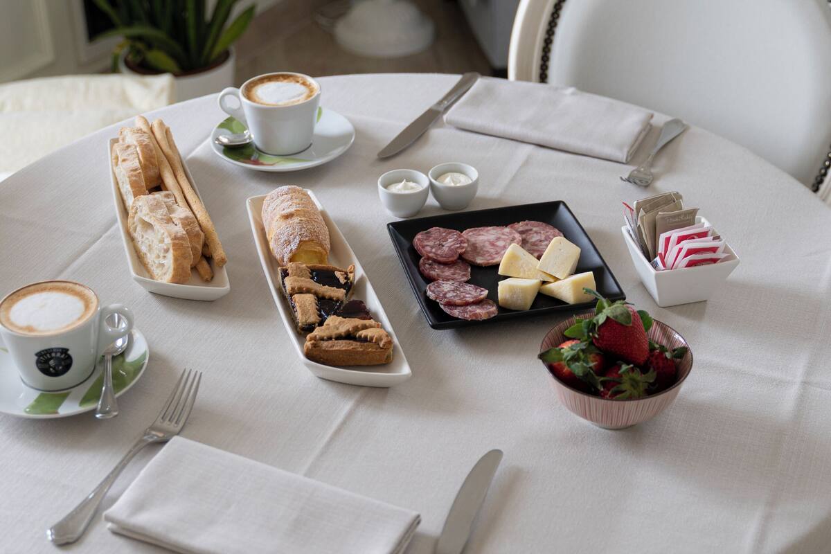 Uma mesa de jantar com diversos tipos de comida, incluindo doces, uma tigela de morangos e um prato de queijos e carnes.