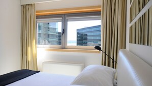 Quarto de hotel com cama, janela com cortinas e vista para prédios.