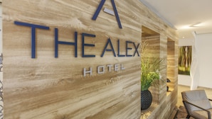 Placa de hotel com o nome 'THE ALEX HOTEL' numa parede de madeira.