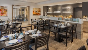 Uma zona de refeições moderna com várias mesas e cadeiras, um buffet central e obras de arte contemporâneas nas paredes.