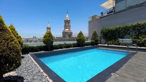 Piscina no terraço com vista clara para um edifício histórico com duas torres.