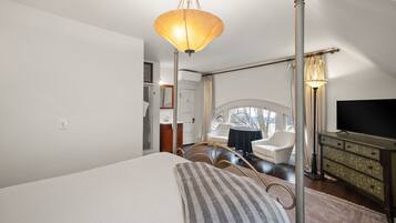 Quarto com cama, televisão, lustre, penteadeira e vista para o exterior.