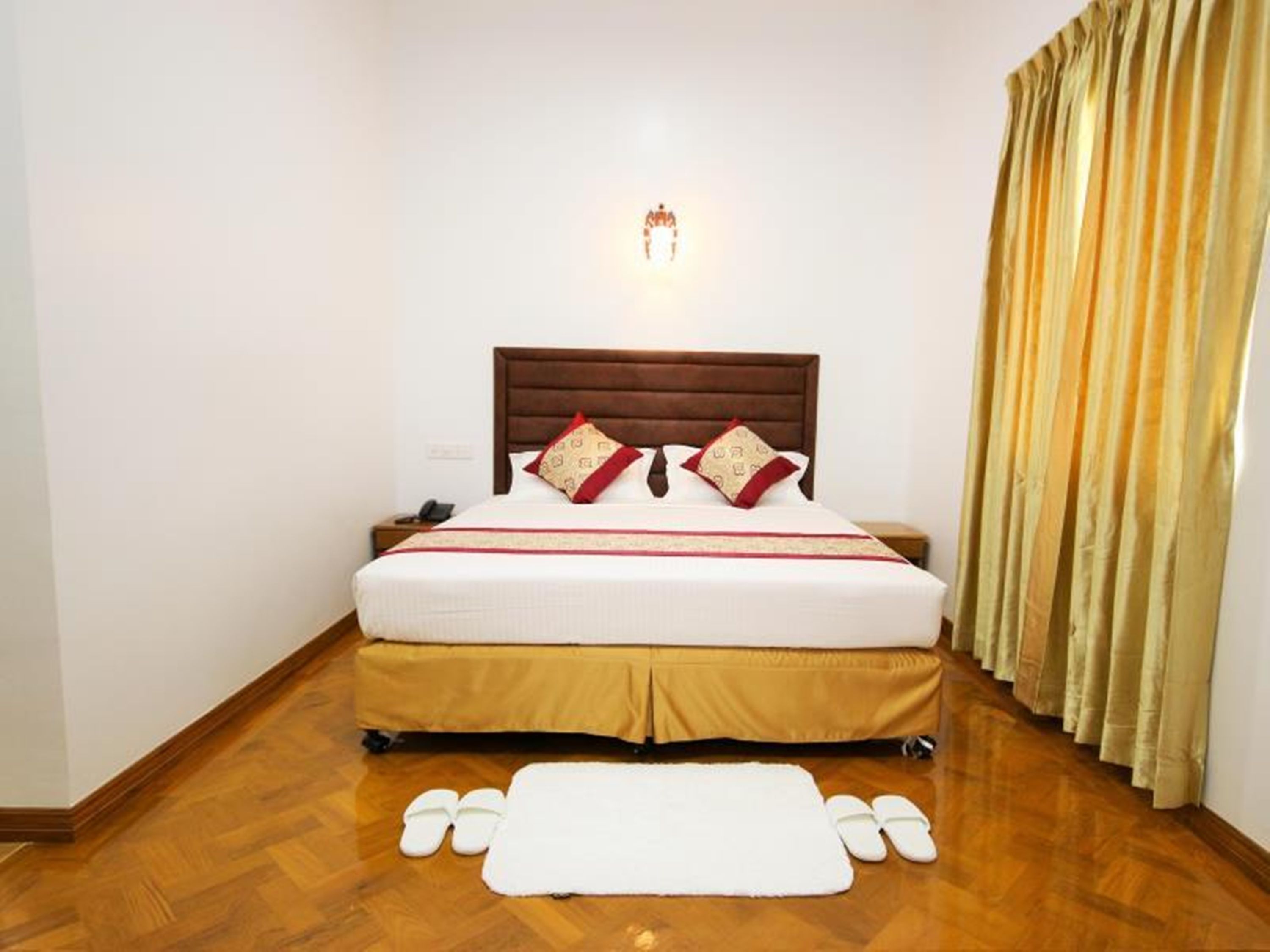 Quarto de hotel bem arrumado com piso de madeira, cama com cabeceira marrom e tapete branco.