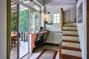 Uma cozinha com escada de madeira, janela com vista para o verde e uma pequena prateleira com utensílios de cozinha.