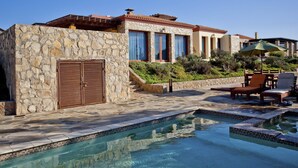 Uma área de piscina com paredes de pedra, uma porta de madeira e mobiliário de exterior.