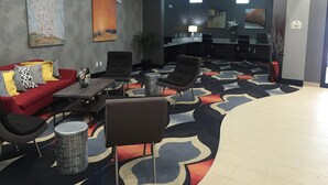 Um lobby moderno com um sofá vermelho, cadeiras pretas, uma mesa de centro e um tapete estampado.
