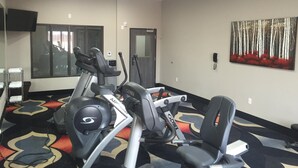 Uma academia com máquinas de cardio, um espelho e um quadro na parede.