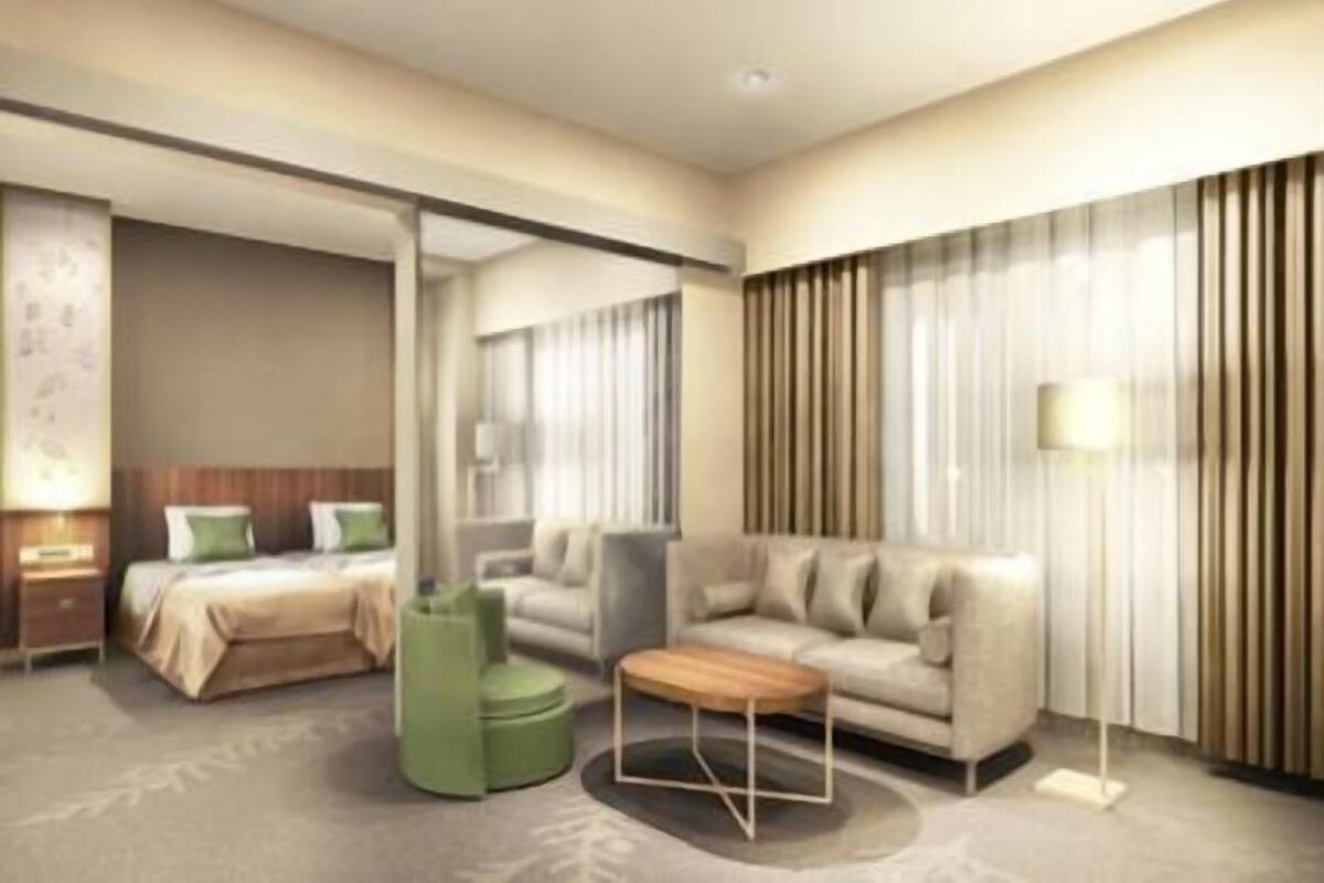 Quarto de hotel moderno com cama, sofá, banquinho verde e abajur.