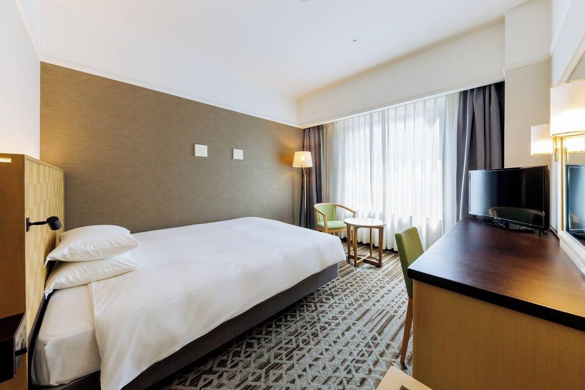 Quarto de hotel com uma cama grande, uma escrivaninha com televisão de tela plana, uma cadeira e uma mesinha.