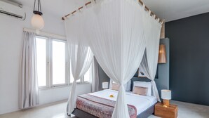 Quarto com cama de dossel, mesa de cabeceira com abajur e vista para o exterior pela janela.
