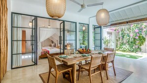 Um quarto espaçoso com uma cama grande, um espaço de refeições com uma mesa posta para quatro pessoas e vista para um jardim exuberante.