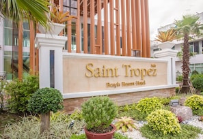 Placa do Hotel Saint Tropez Beach Resort com design moderno, rodeada por paisagismo bem cuidado e palmeiras.