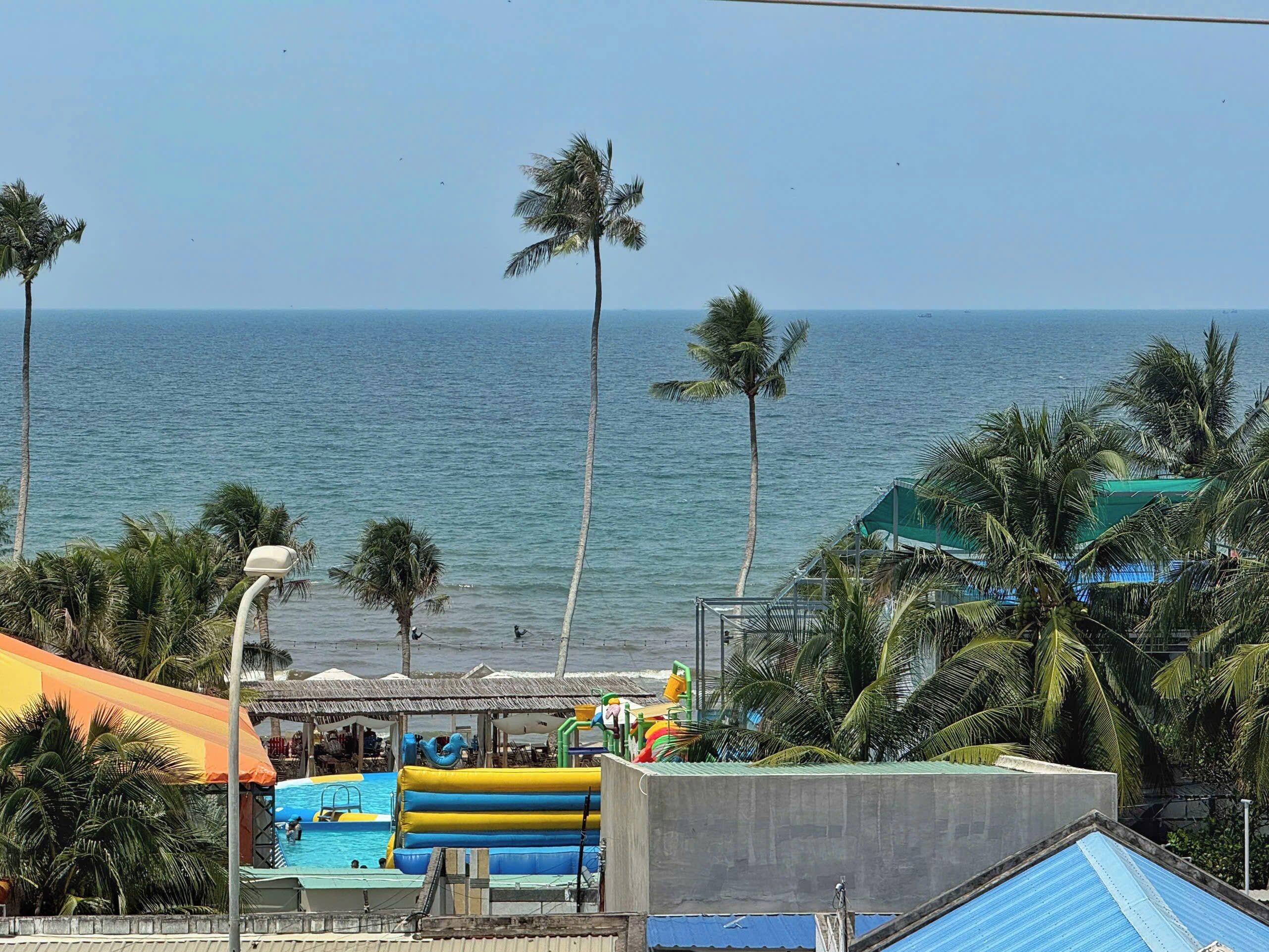 Vista à beira-mar com área de piscina, palmeiras e oceano visível.