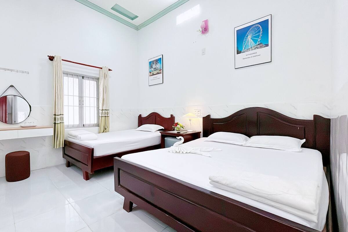 Quarto de hotel com duas camas, mesa de cabeceira com luminária, espelho e janela com cortinas.