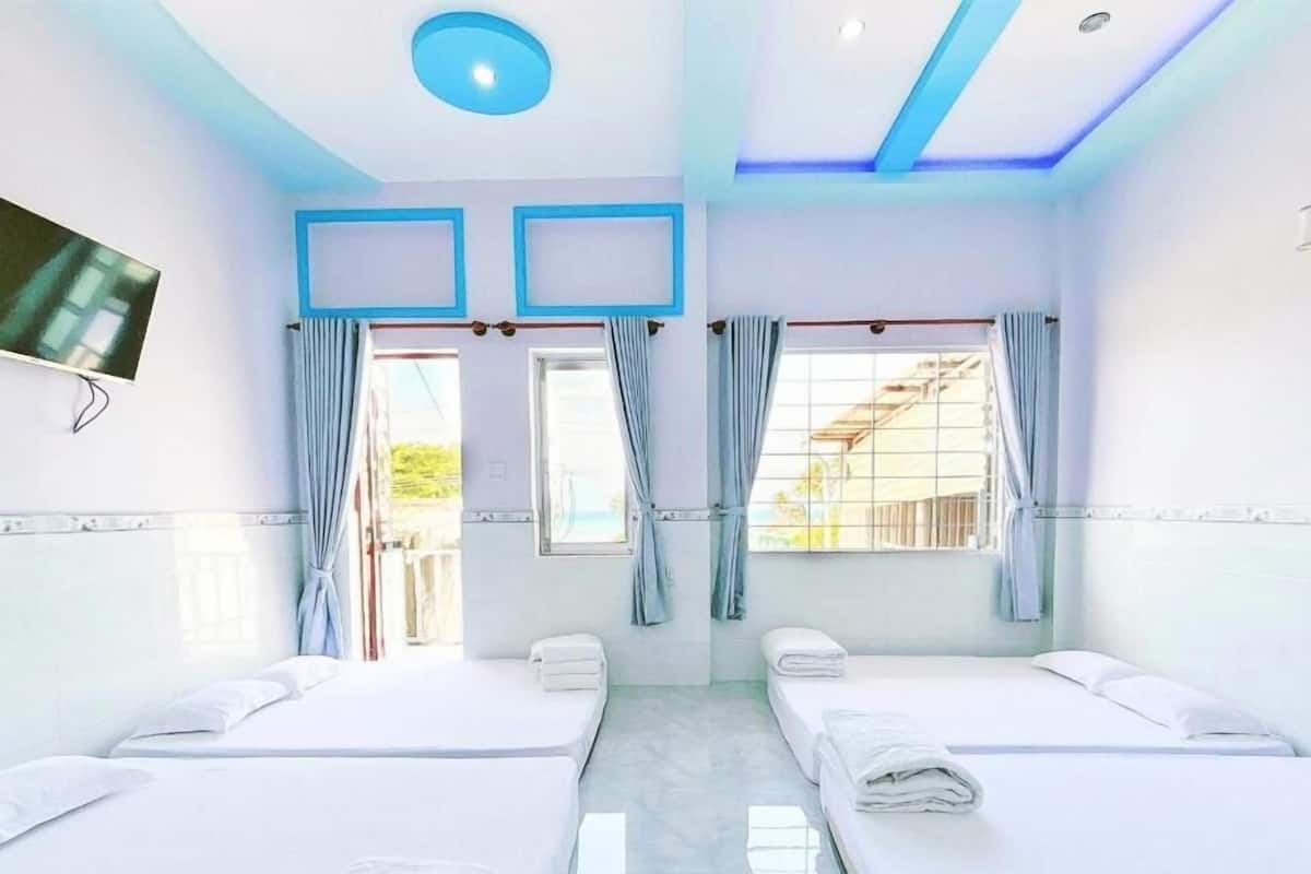 Quarto de hotel com duas camas, televisão presa na parede e uma janela grande com cortinas.
